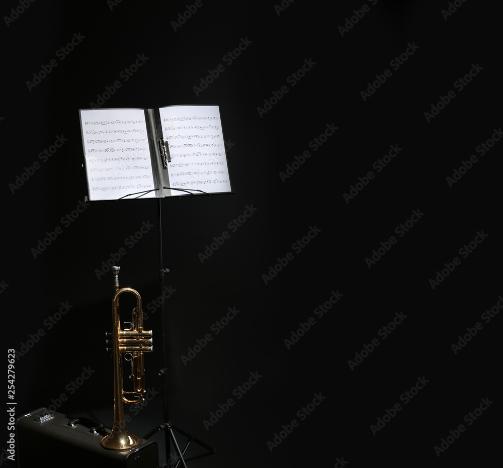 Trumpet, case and note stand with music sheets on black background ...