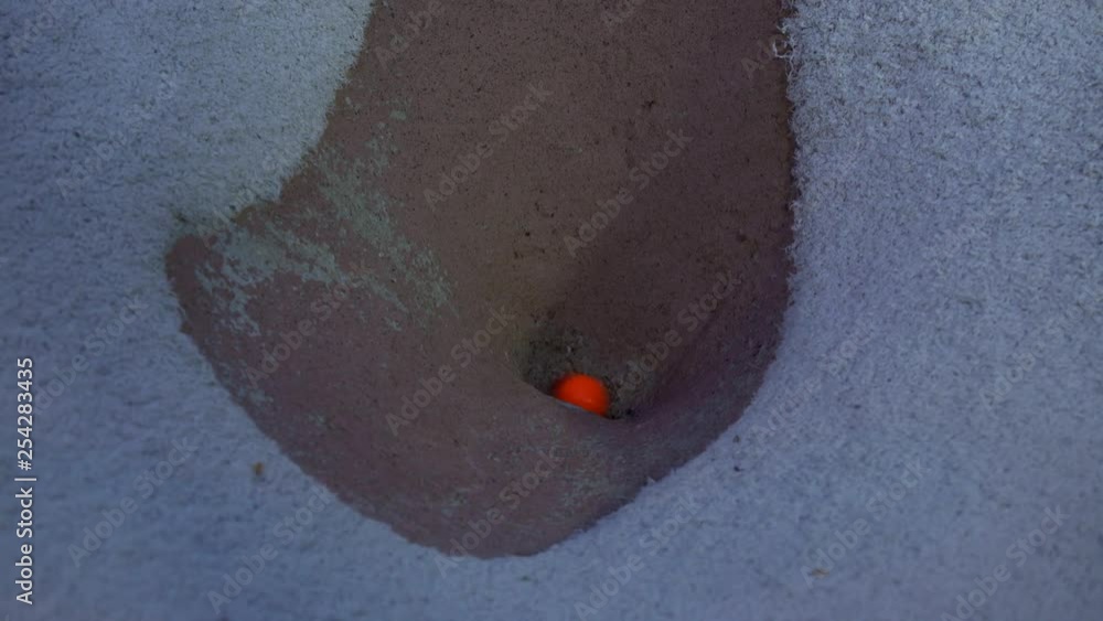 An orange ball rolling into an obstacle at a mini golf course and ...