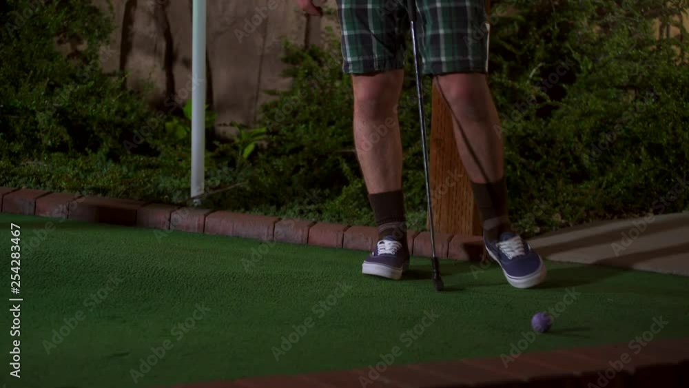A close up of a purple mini golf ball getting hit with a club and the ...