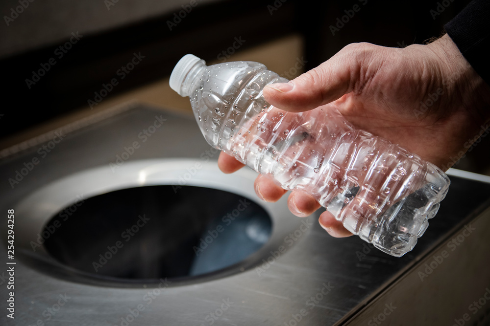 Hand throwing disposable plastic water bottle into trash or recycling ...