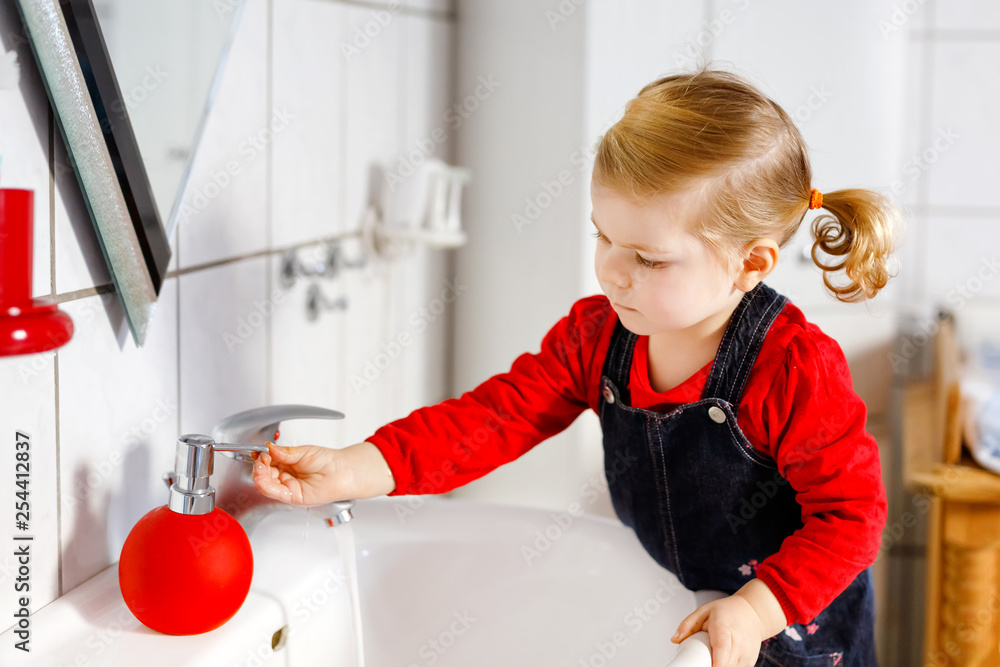 Cute little toddler girl washing hands with soap and water in bathroom ...