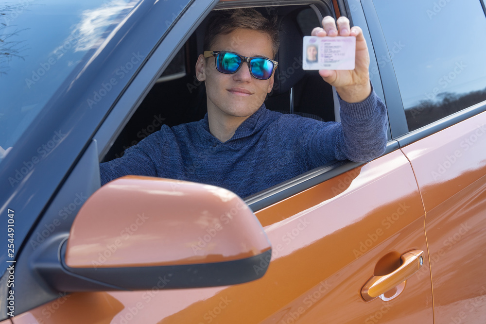 Happy teenager is showing his driving license from open car window ...