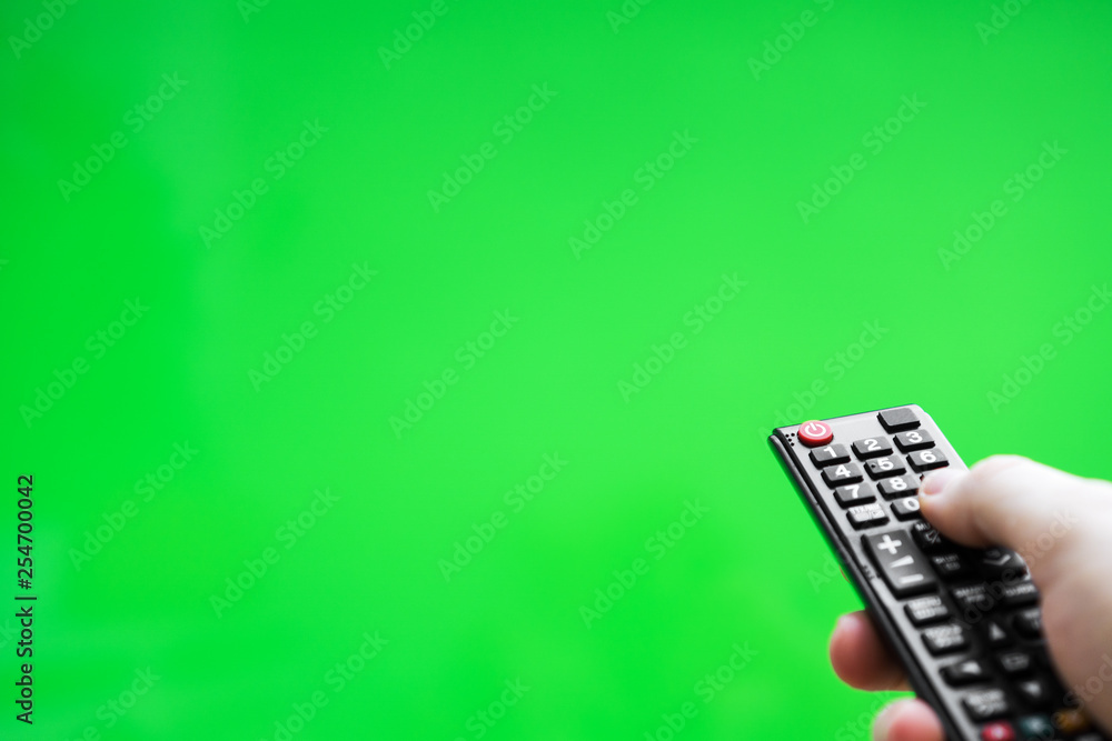 Male hand with TV remote control over green screen. Place for your ...