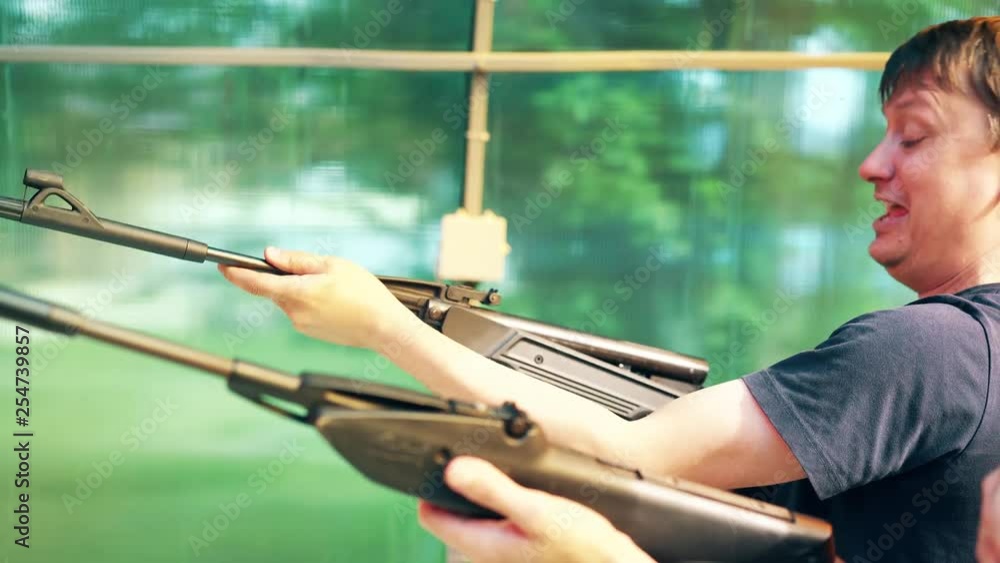 Close-up: Young guys shoot at shooting range from pneumatic guns, one ...