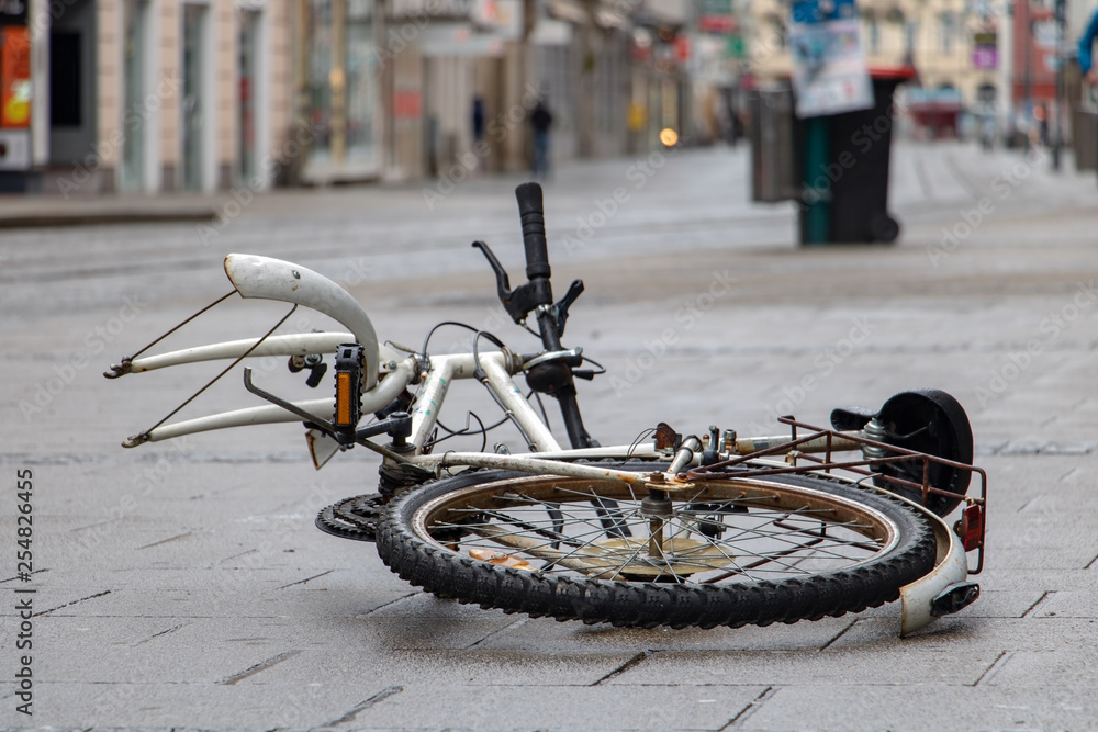 The damaged bicycle lying on the street in the city center. The ...