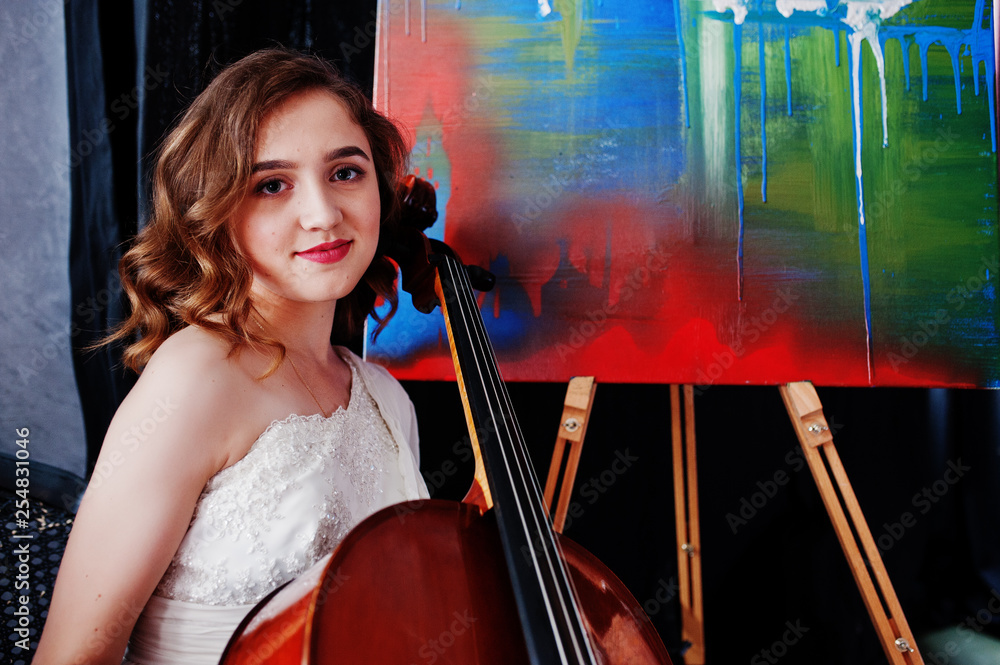 Pretty young gilrl musician in white dress with double bass next to her ...