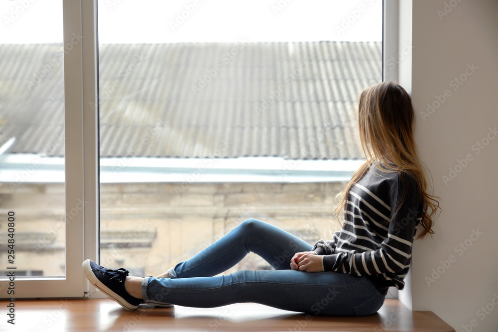 Beautiful young woman sitting on window sill Stock Photo | Adobe Stock