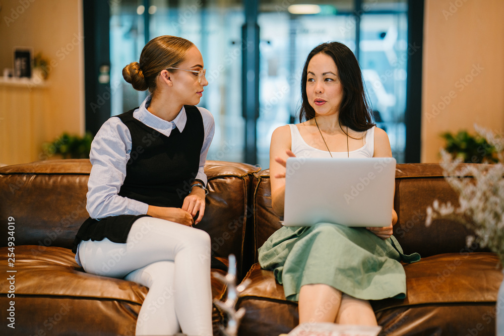 Two beautiful ladies discussing a document inside a cafe. They are ...