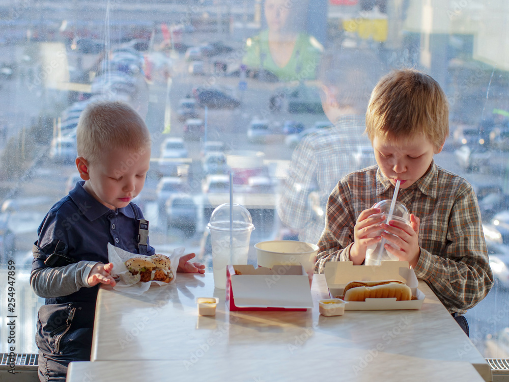 Children have lunch in fast food cafe. Boys drink lemonade and eat ...