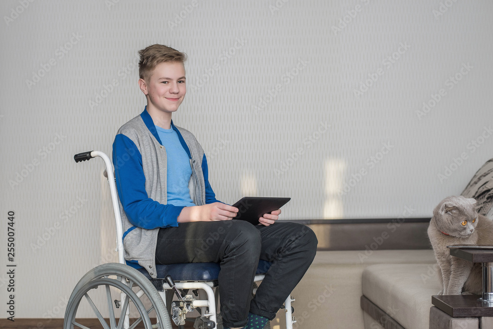 teen boy student sitting in a wheelchair while using a tablet at home ...