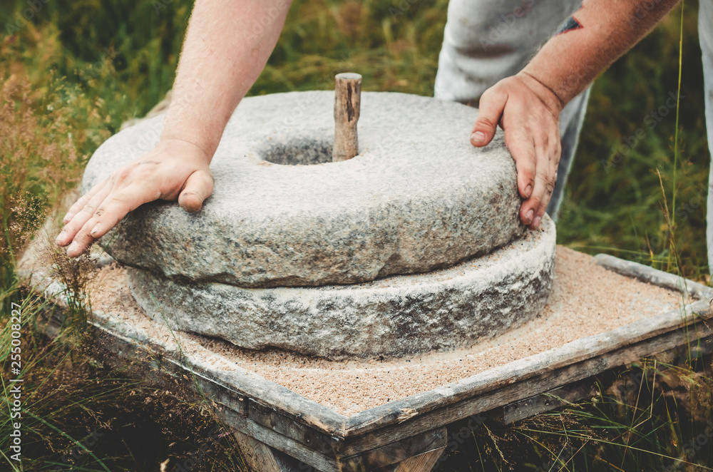 The ancient quern stone hand mill with grain. The man grinds the grain ...