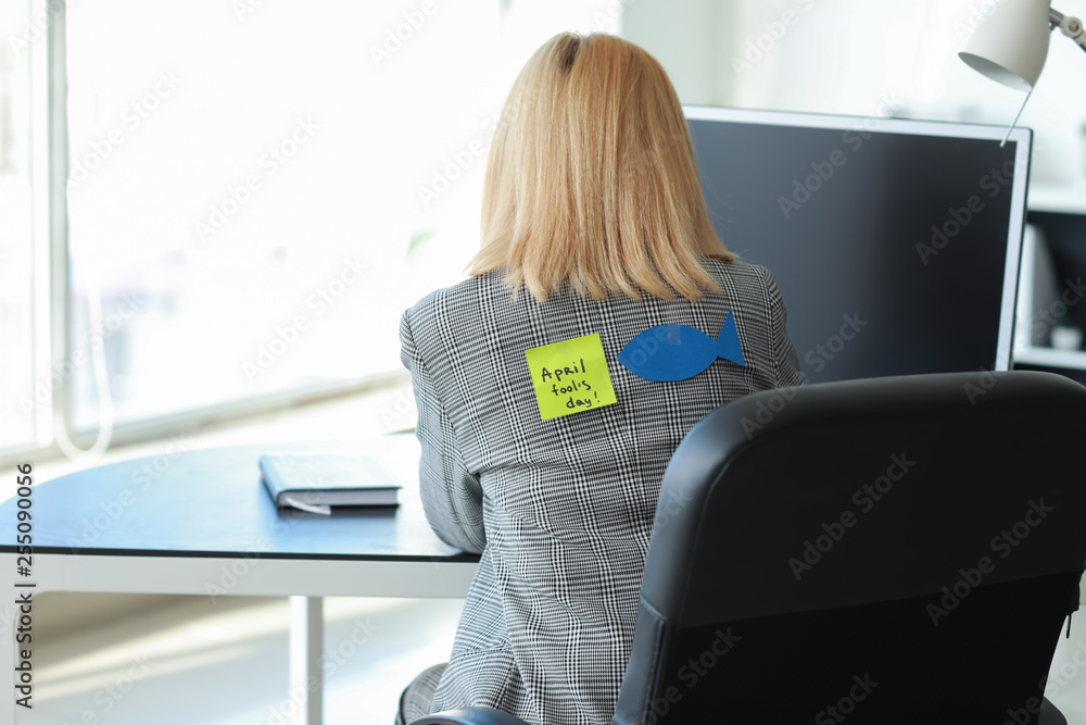 Sticky note with text APRIL FOOL'S DAY and paper fish on back of woman ...