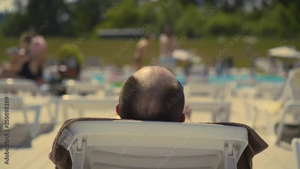 Vidéo Stock Back view, Close-up: Bald Italian man is lying on the beach ...