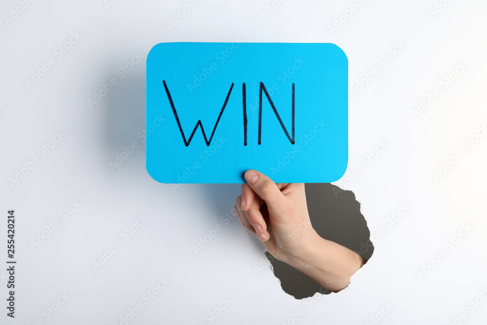 Woman showing card with word WIN through hole in torn white paper ...