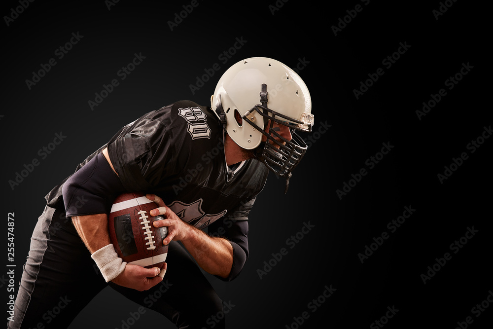 American football player in dark uniform with the ball is preparing to ...