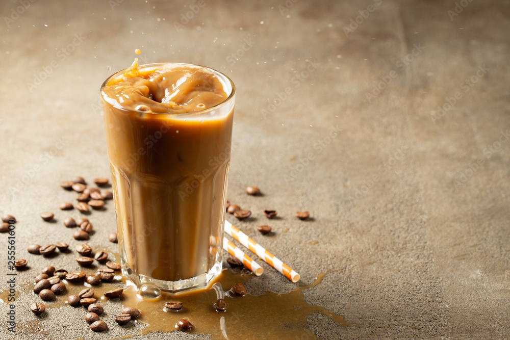 Iced latte coffee splash with ice cubes and roasted beans on a dark ...