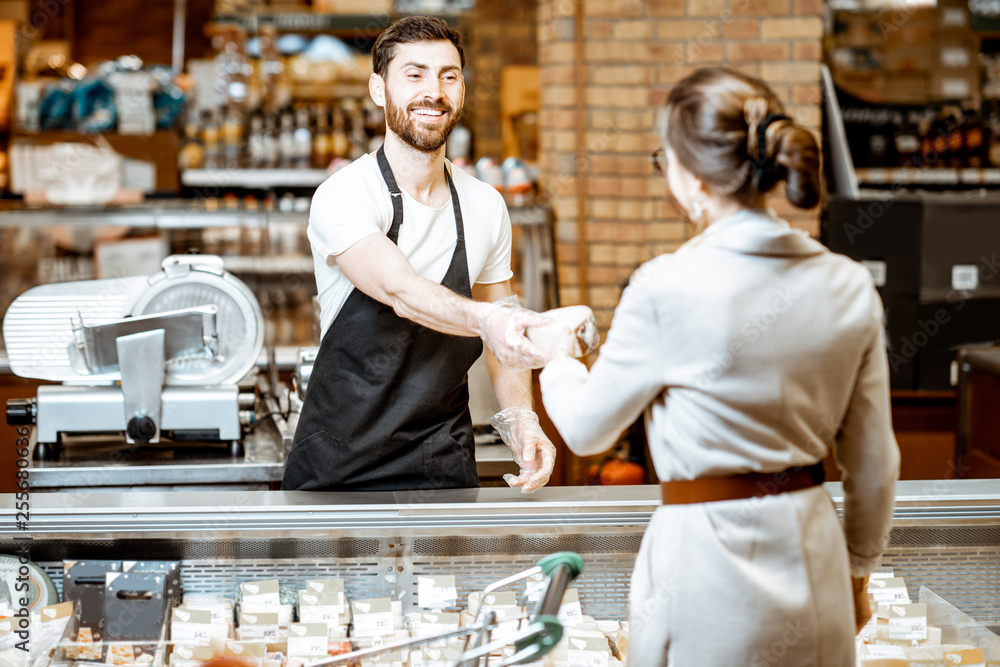 Handsome shop worker selling cheese for a young woman client standing ...