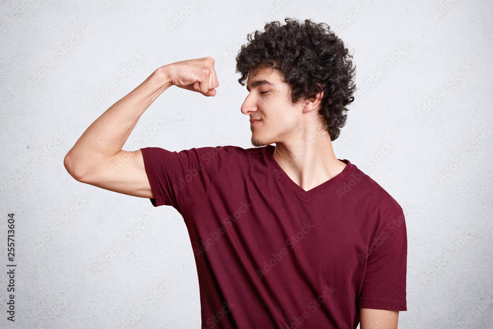 Positive dark haired teenager, dressed casually, shows biceps with ...