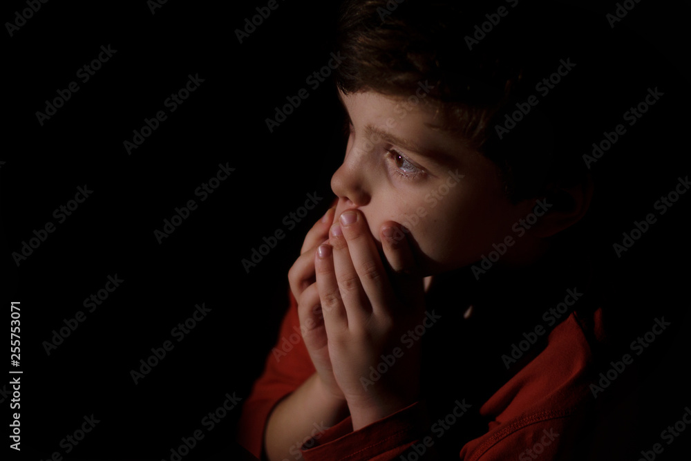 Portrait in the dark of a young scared sad boy of seven years scared ...