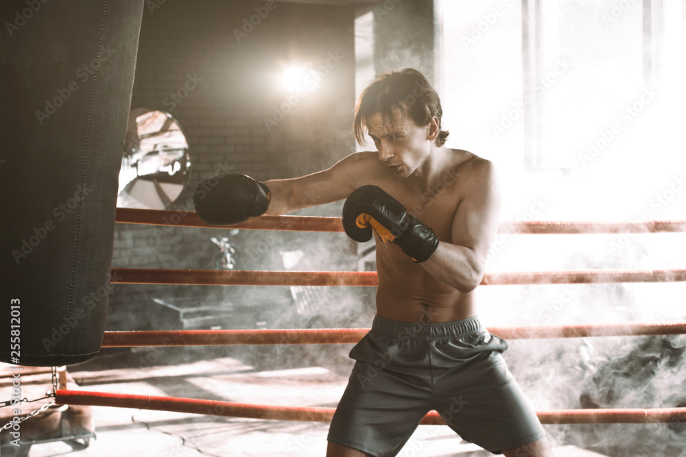 Male Caucasian boxer punching a boxing bag in boxing studio with bright ...