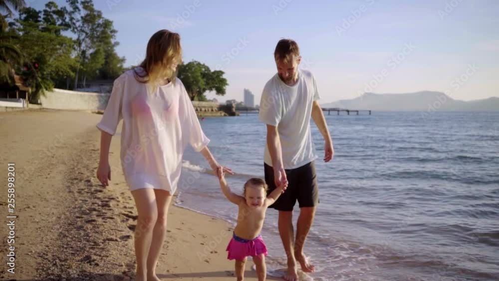 Happy family at the beach, holding hands, waving a little girl around ...