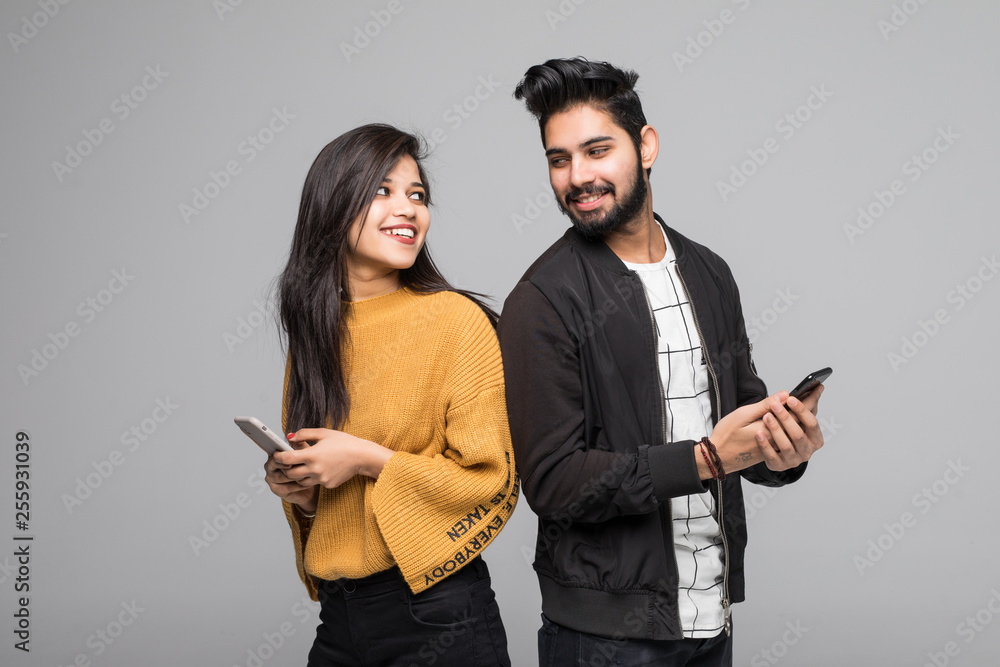 Beautiful young indian couple holding mobile phones and standing back ...