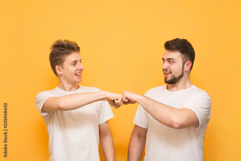 Portrait of a two happy young men giving fist bump isolated over yellow ...