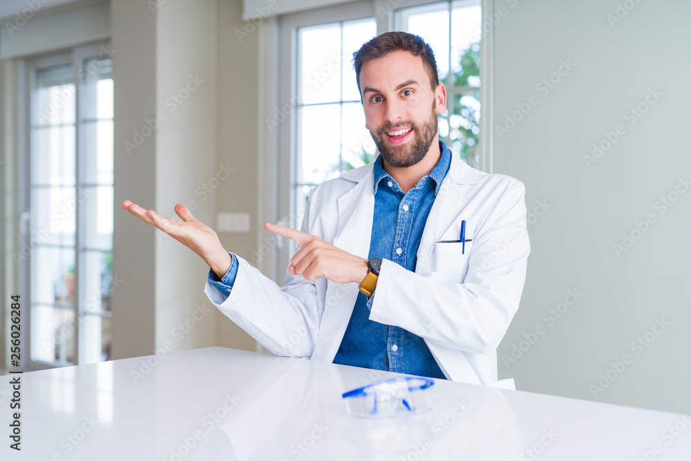 Handsome scientist man wearing white robe and safety glasses amazed and ...