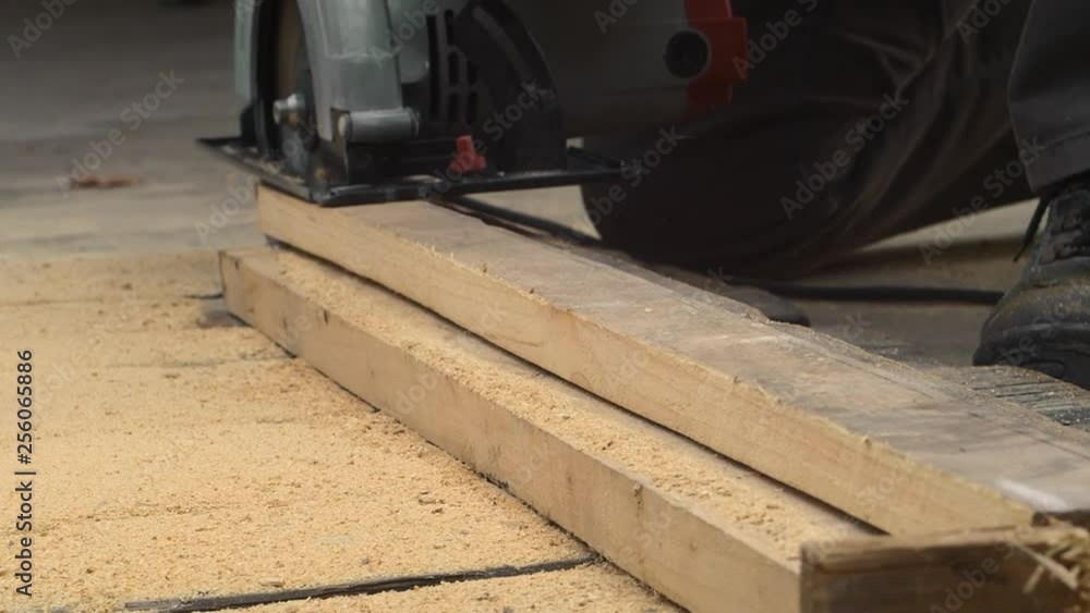 Worker with saw cuts wood Worker in uniform with a circular saw cuts a ...