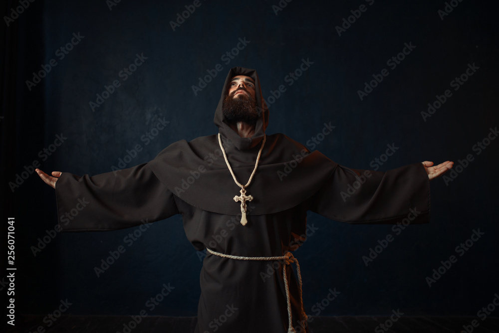 Monk in black robe with hood kneeling and praying Stock Photo | Adobe Stock