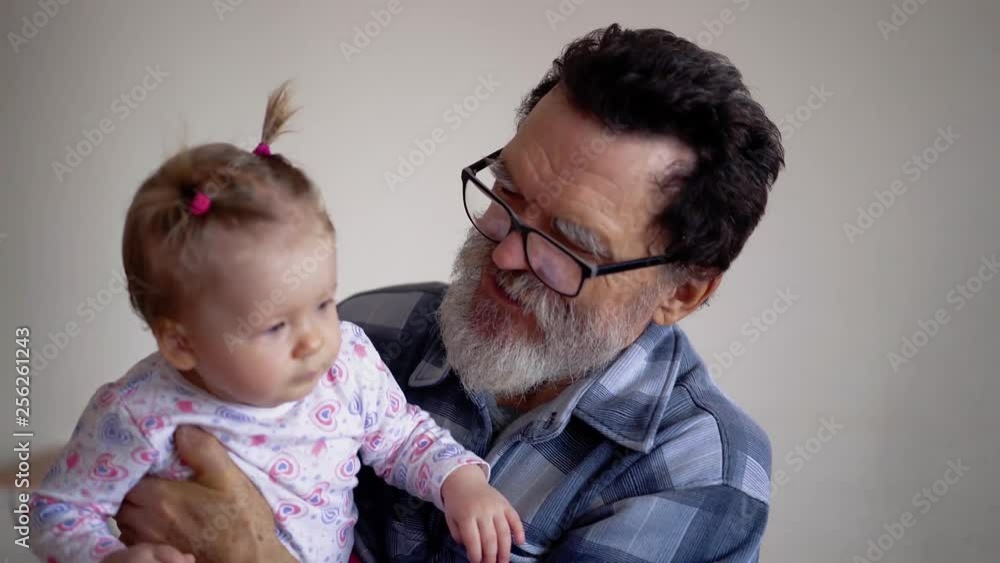 Grandfather with a beard, wearing glasses, playing with a little ...