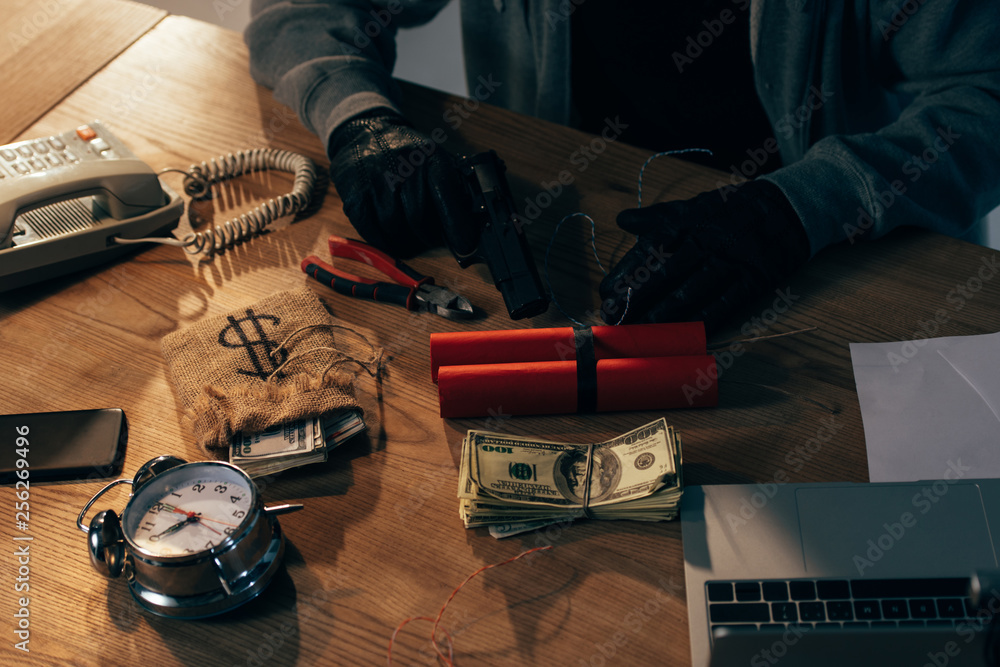 Partial view of terrorist in black gloves with dynamite, gun and dollar ...