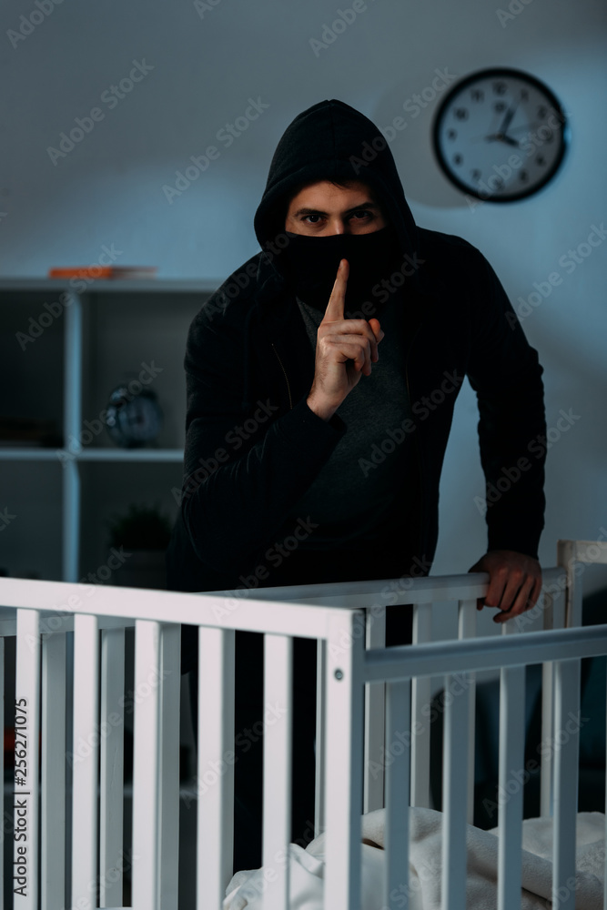 Kidnapper in mask standing near crib and showing hush sign Stock Photo ...