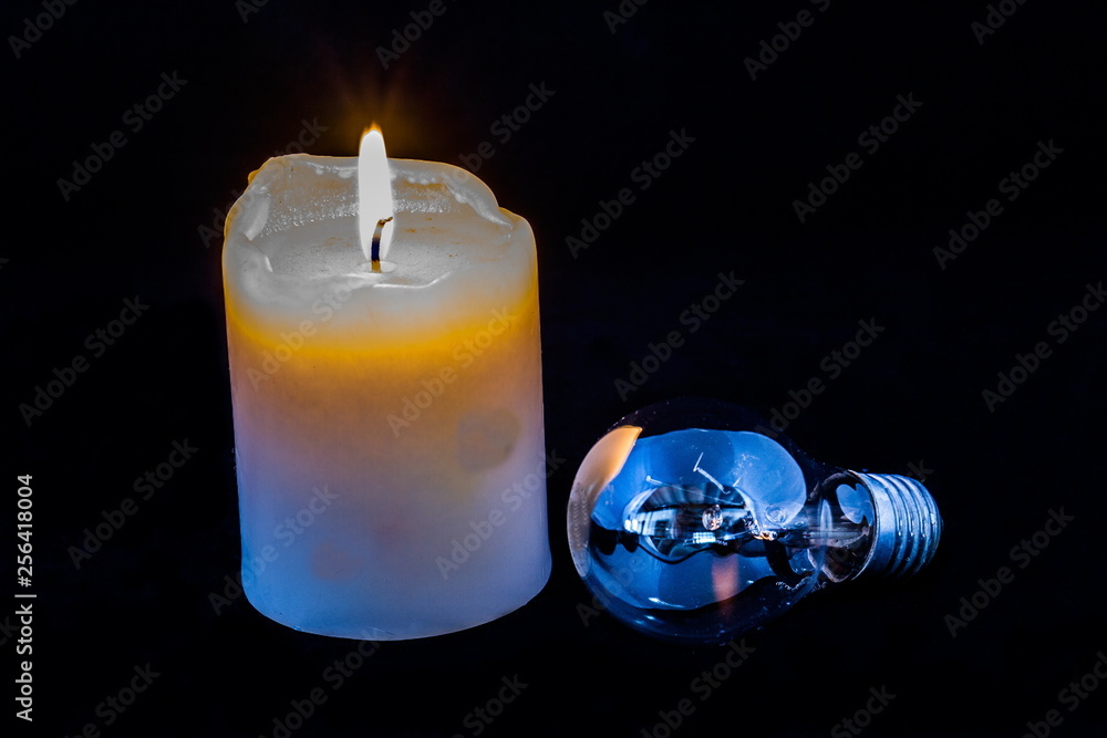 Burning candle and an electric light globe isolated on a black ...