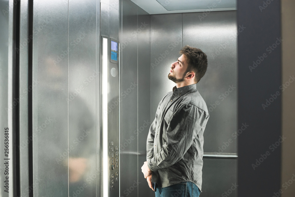 Man with a beard stands in the elevator and looks at the screen with a ...