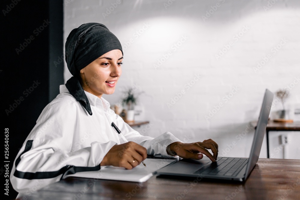 Muslim woman in hijab working remotely on a laptop sitting in a cafe ...