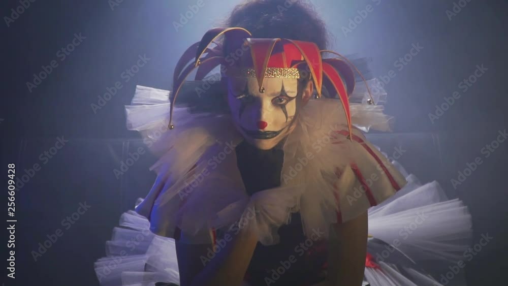 Scary woman clown with white and black makeup is sitting with mad look ...