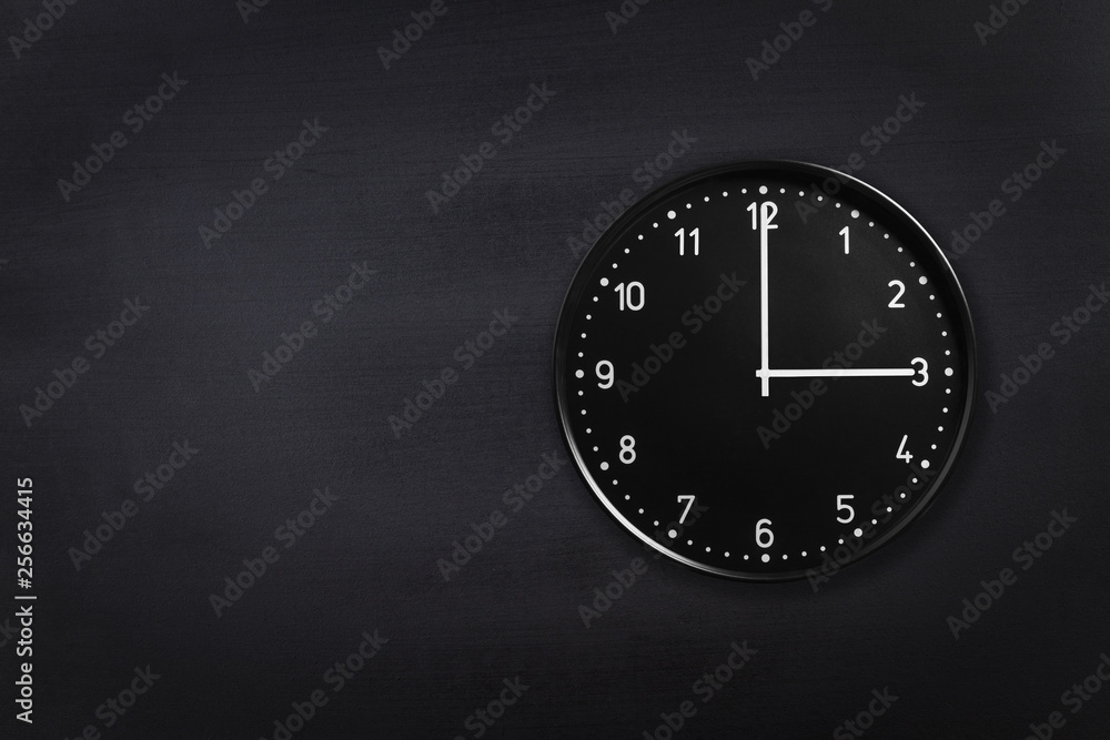 Black wall clock showing three o'clock on black chalkboard background ...