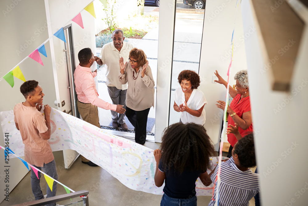 Three generation family throwing a surprise party welcoming guests at ...