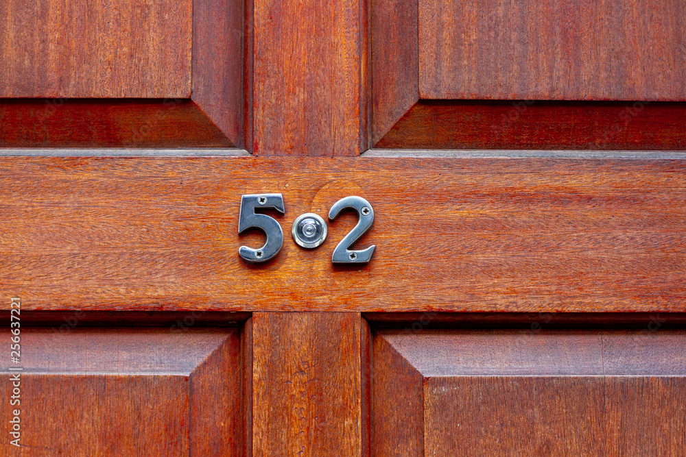 House number fifty-two on a red wooden door with natural grain with the ...