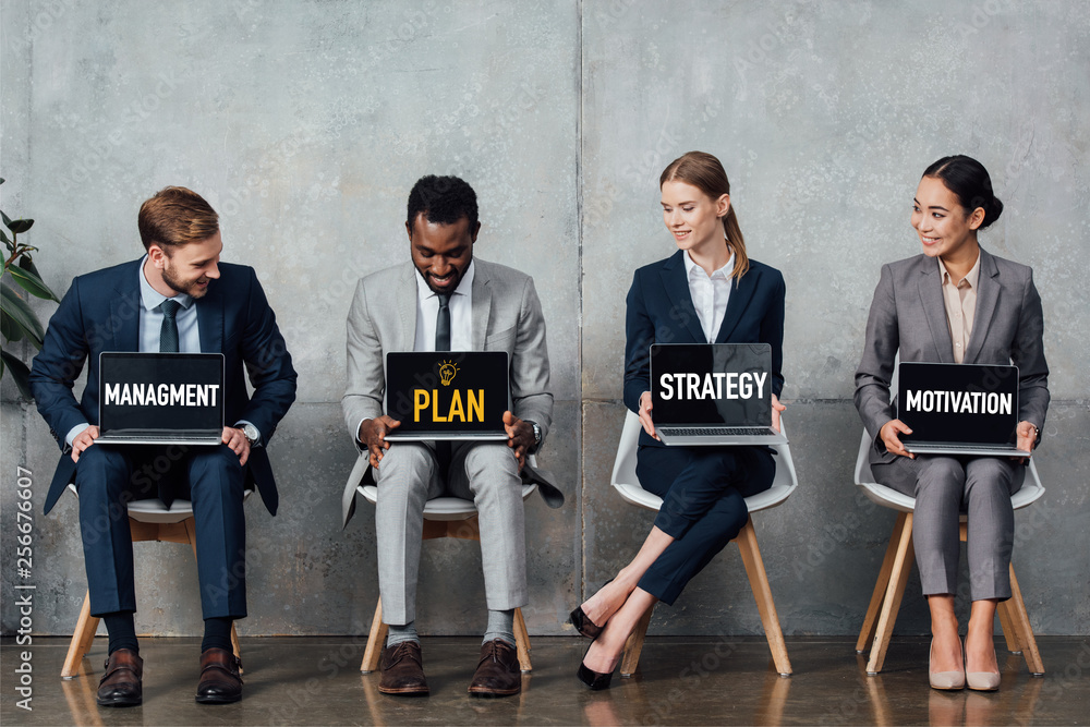 smiling multiethnic businesspeople sitting on chairs and holding ...
