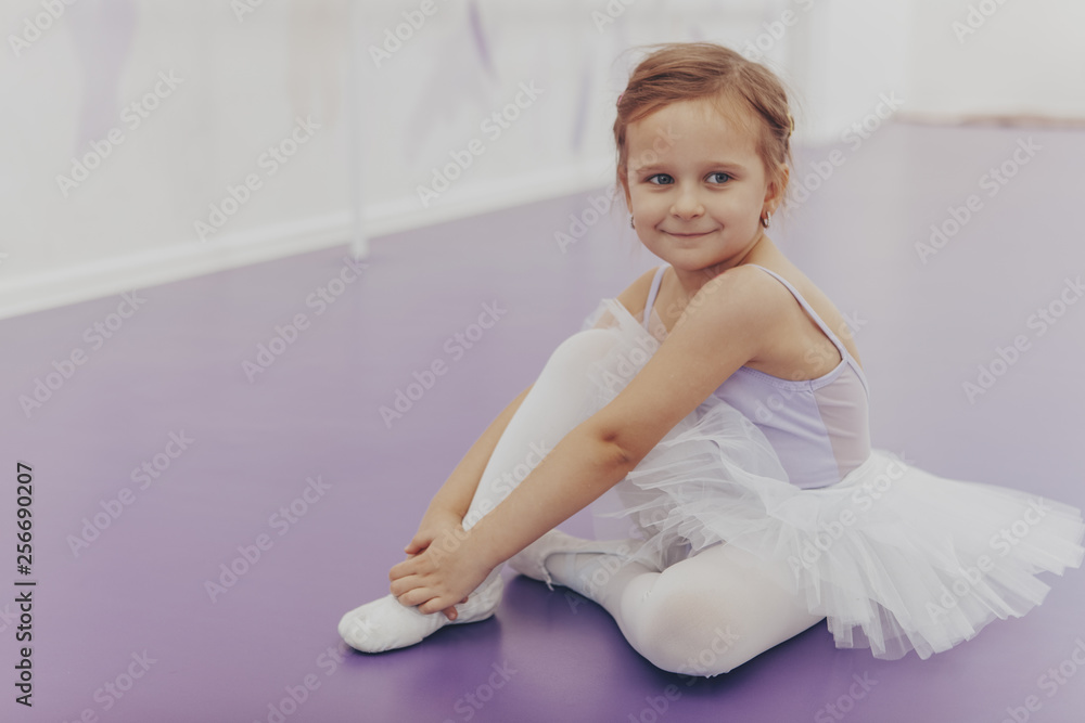 Cute little happy ballerina smiling to the camera sitting on the floor ...