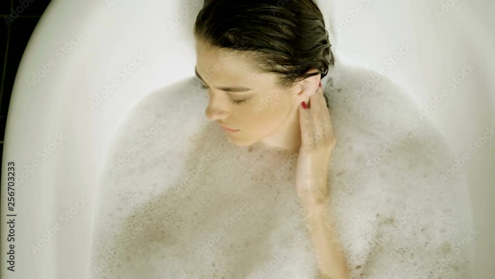 Top view of young brunette woman taking a bubble bath in bathtub. She ...