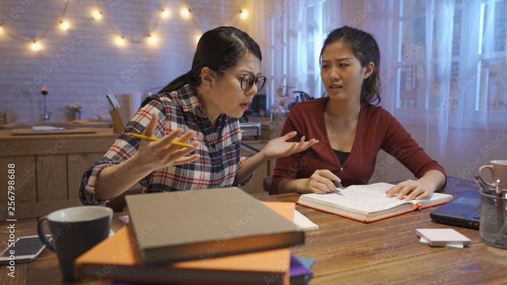 two asian woman sitting at laptop computer at wooden kitchen table ...
