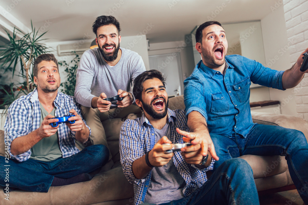 Smiling male friends playing video games at home and having fun. Stock ...