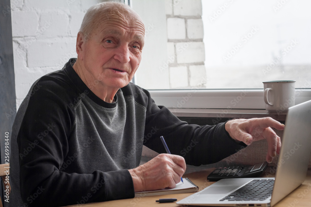 An old man points his finger at the laptop screen and looks at the ...