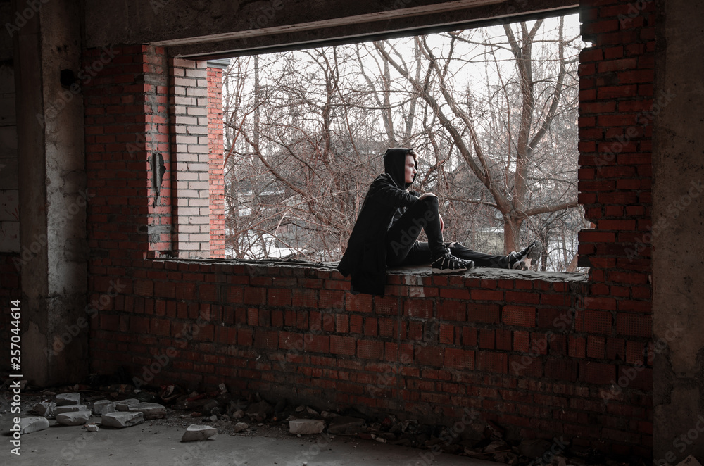Sad reflective teenager sitting on the windowsill in an unfinished ...
