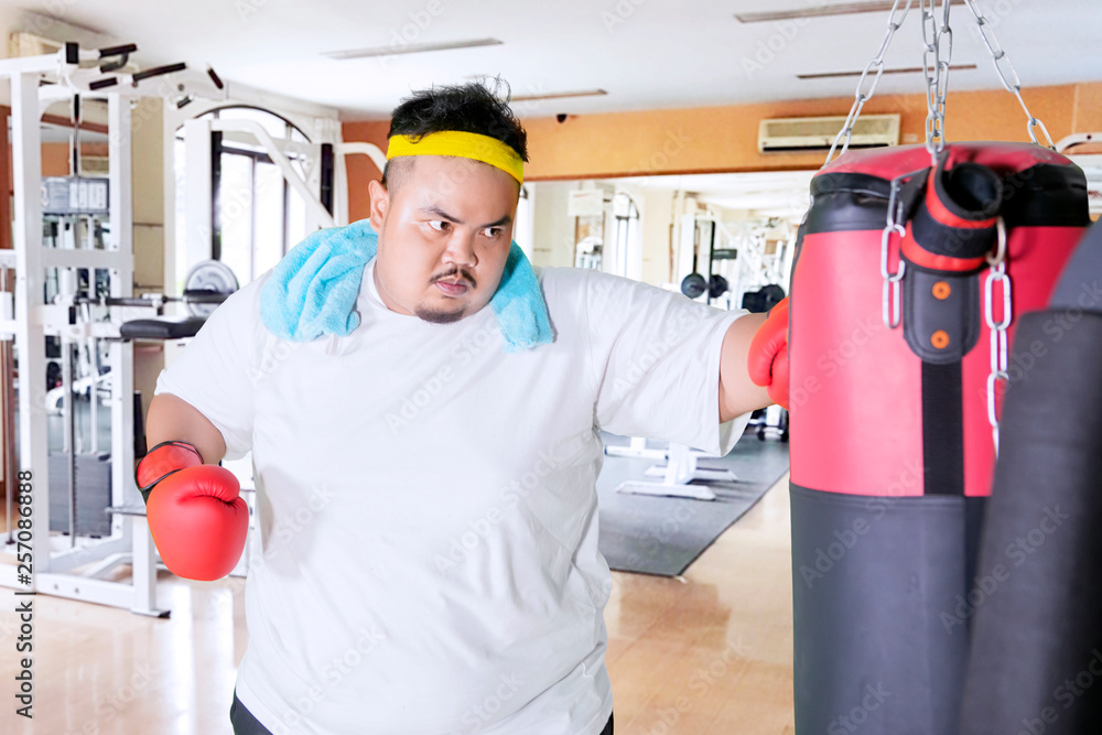Fat man punches a boxing sack in gym center Stock Photo | Adobe Stock