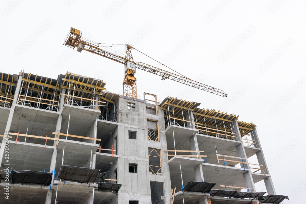 High-rise building crane with a long arrow of yellow color against the ...