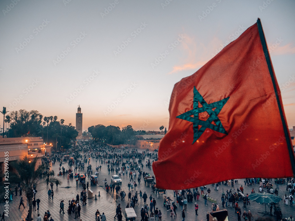 The waving flag of Morocco and the famous minaret of Marrakech at ...